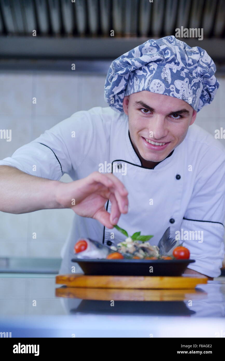 Handsome chef dressed in white uniform decorating pasta salad and ...