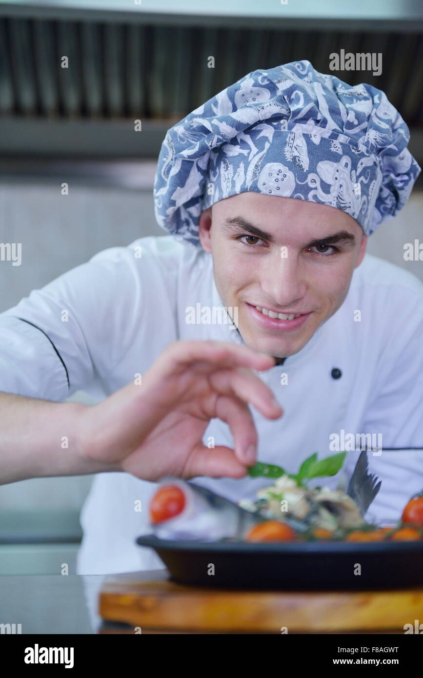 Handsome chef dressed in white uniform decorating pasta salad and ...