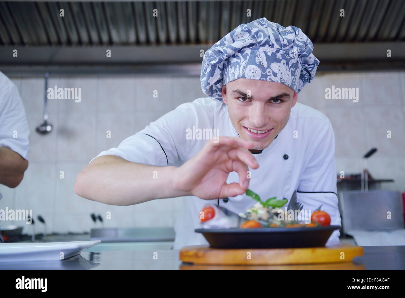 Handsome chef dressed in white uniform decorating pasta salad and ...