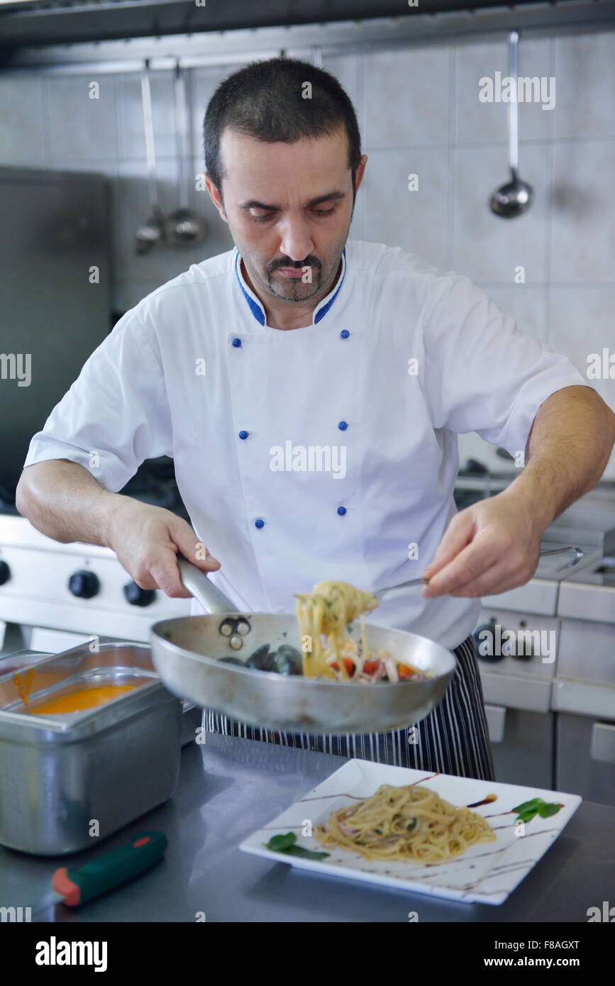 Handsome chef dressed in white uniform decorating pasta salad and ...