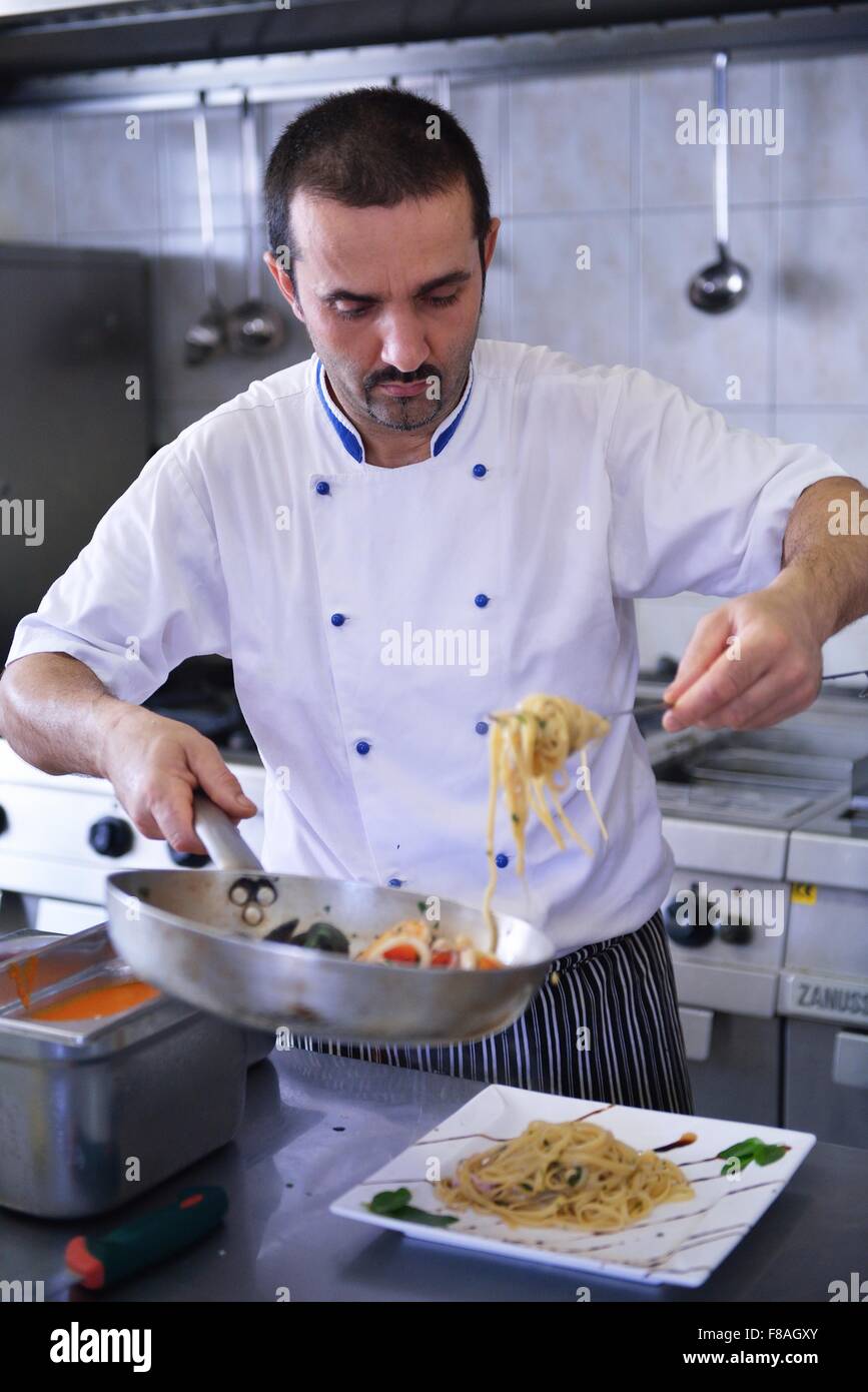 Handsome chef dressed in white uniform decorating pasta salad and ...