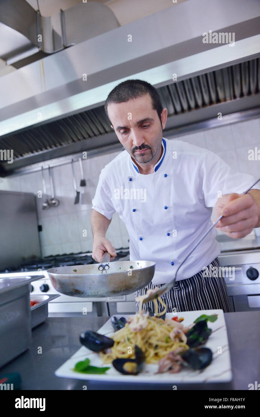 Handsome chef dressed in white uniform decorating pasta salad and ...