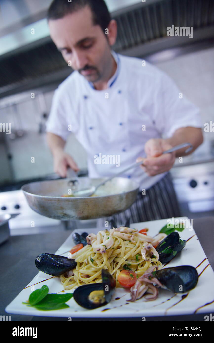 Handsome chef dressed in white uniform decorating pasta salad and ...
