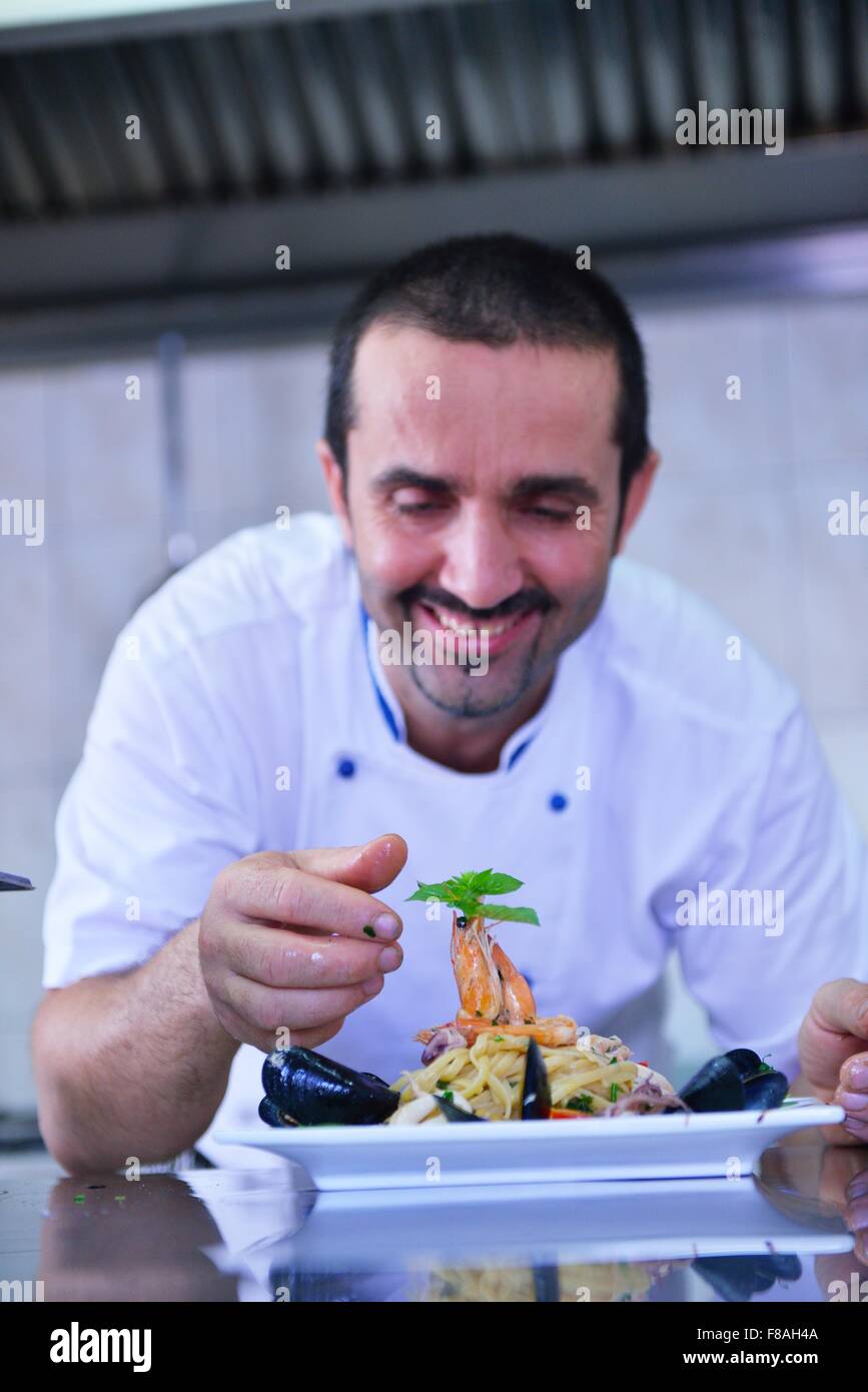 Handsome chef dressed in white uniform decorating pasta salad and ...