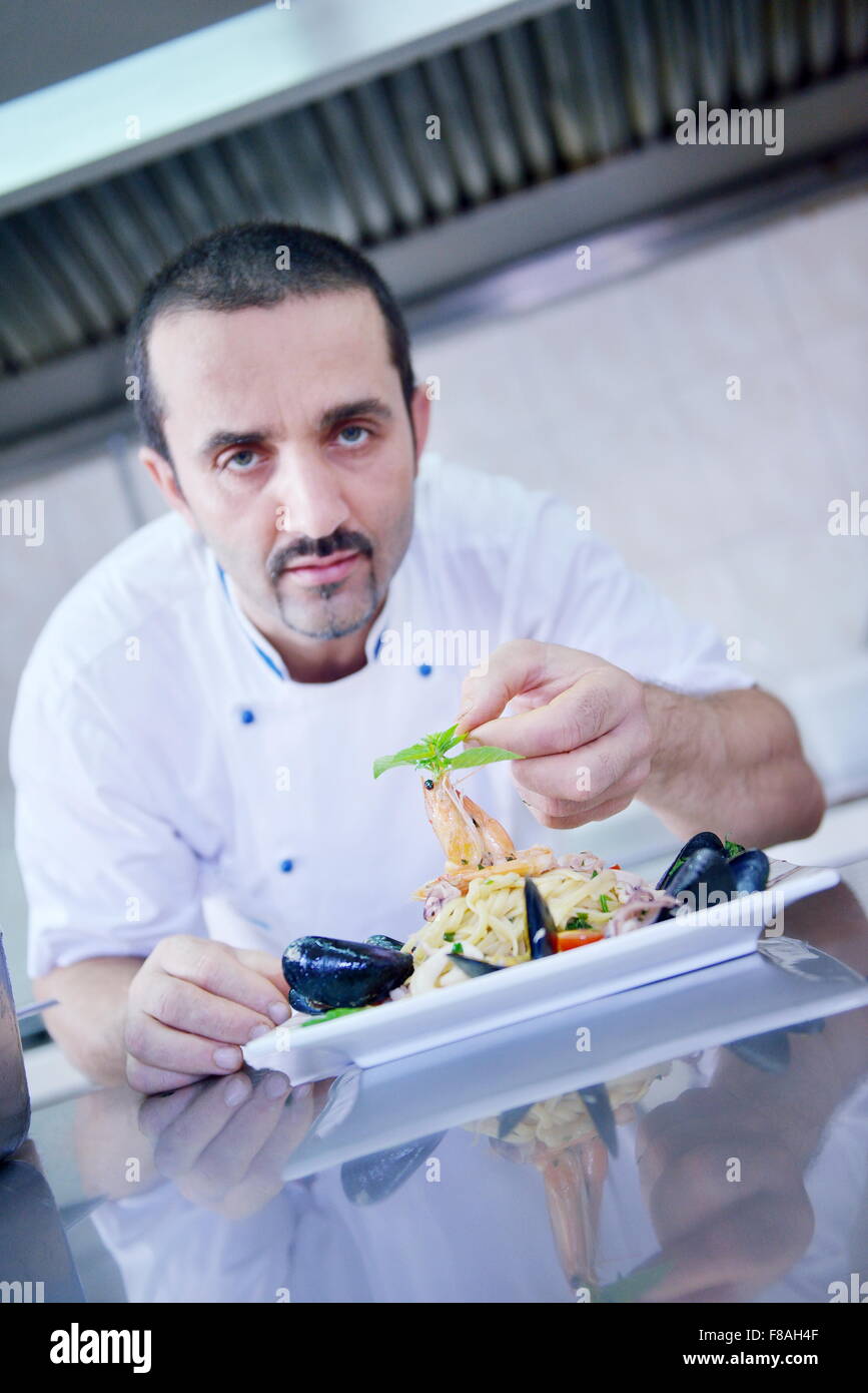 Handsome chef dressed in white uniform decorating pasta salad and ...