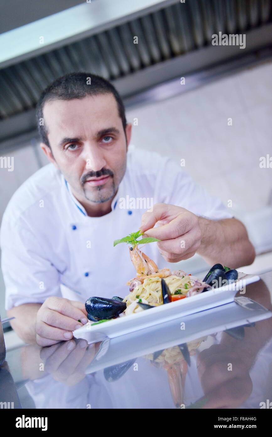 Handsome chef dressed in white uniform decorating pasta salad and ...