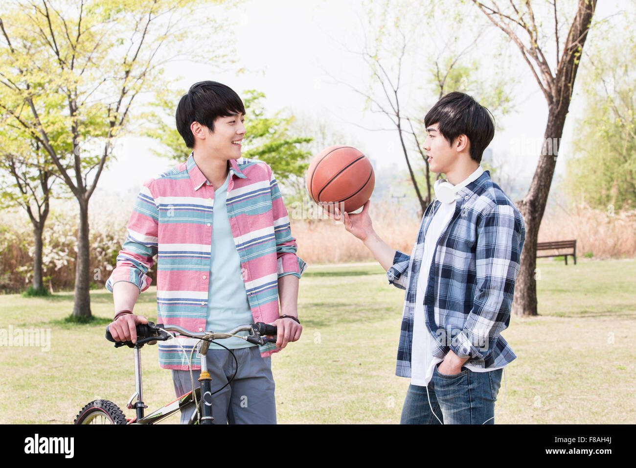 Two male friends standing next to each other and smiling at the park ...