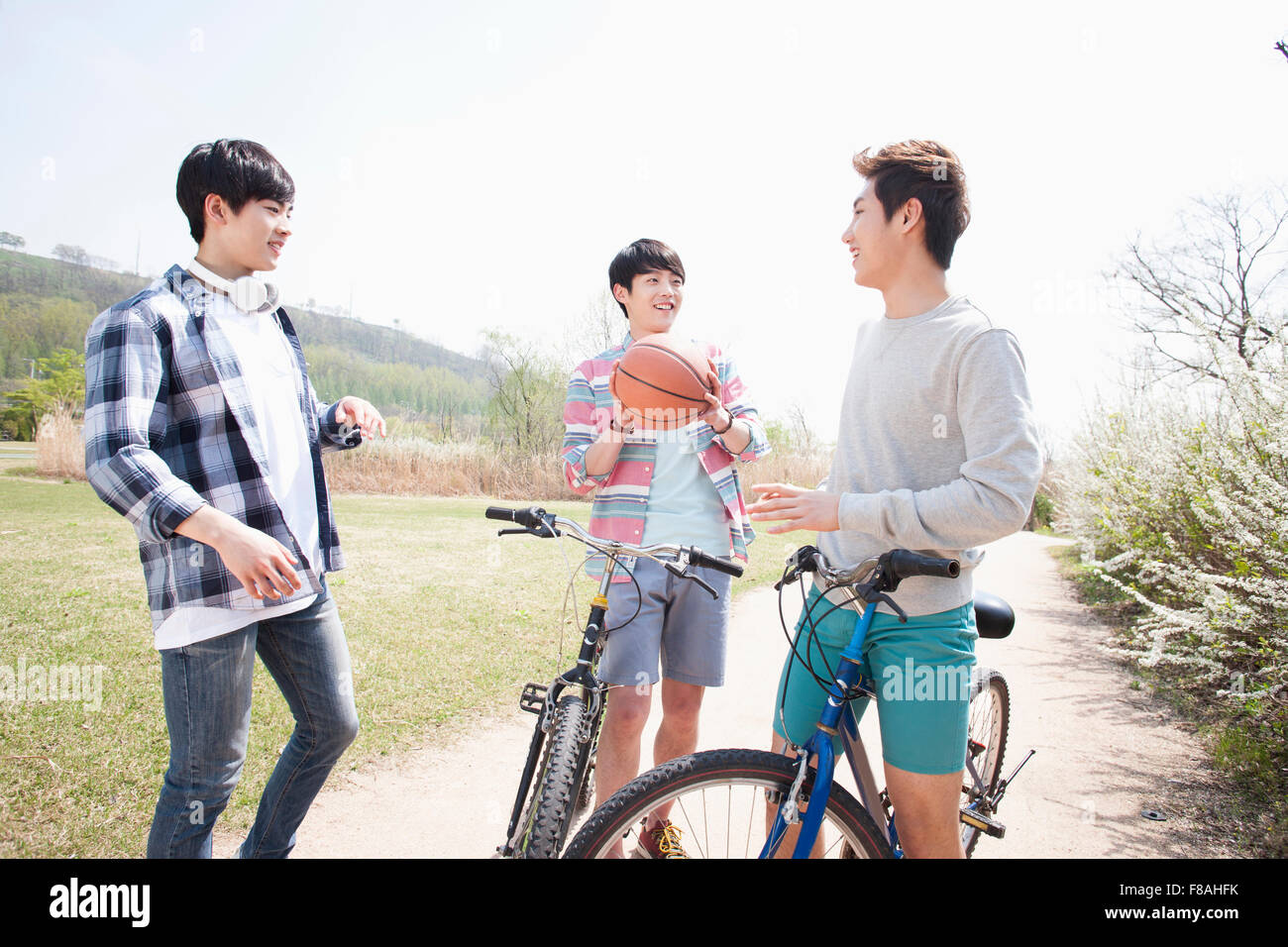 Three young men having fun with their bikes and a basketball together ...