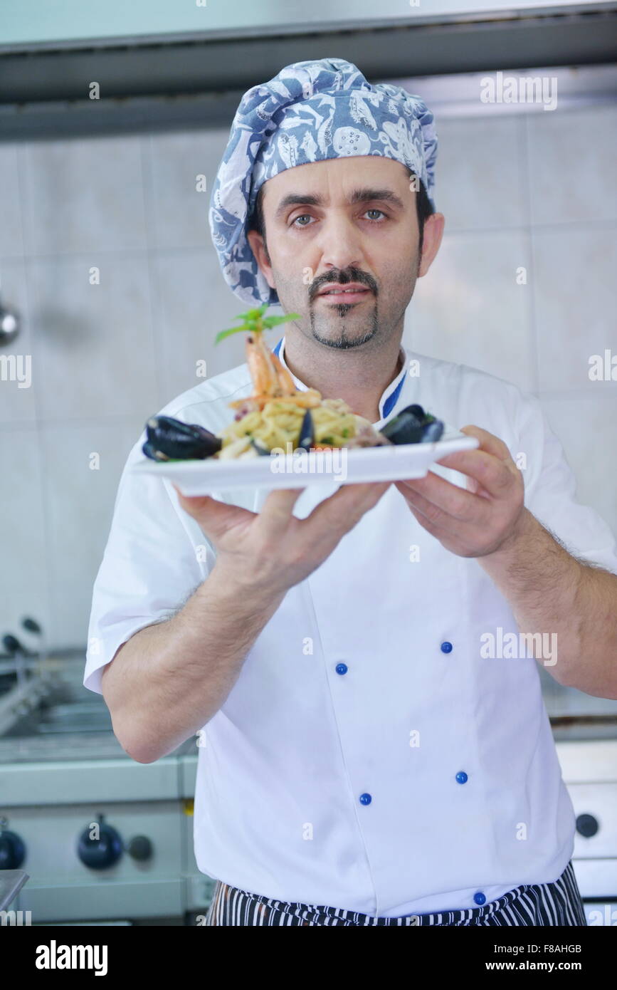 Handsome chef dressed in white uniform decorating pasta salad and ...