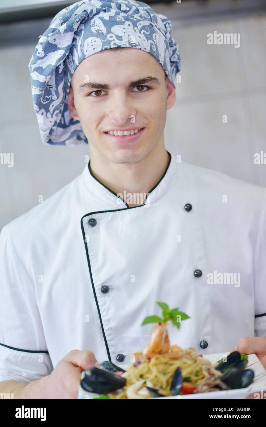 Handsome chef dressed in white uniform decorating pasta salad and ...