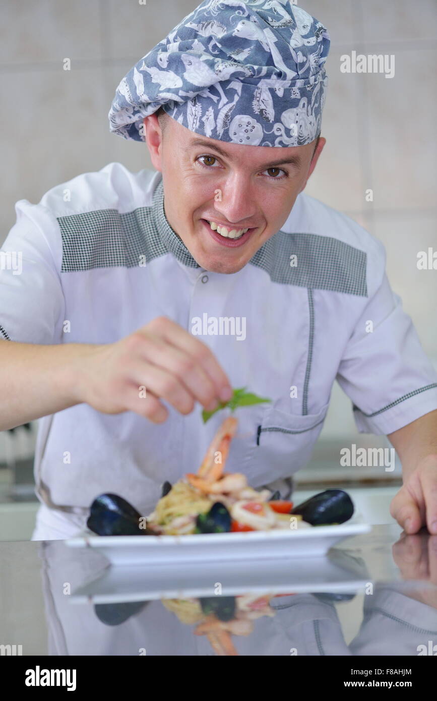 Handsome chef dressed in white uniform decorating pasta salad and ...