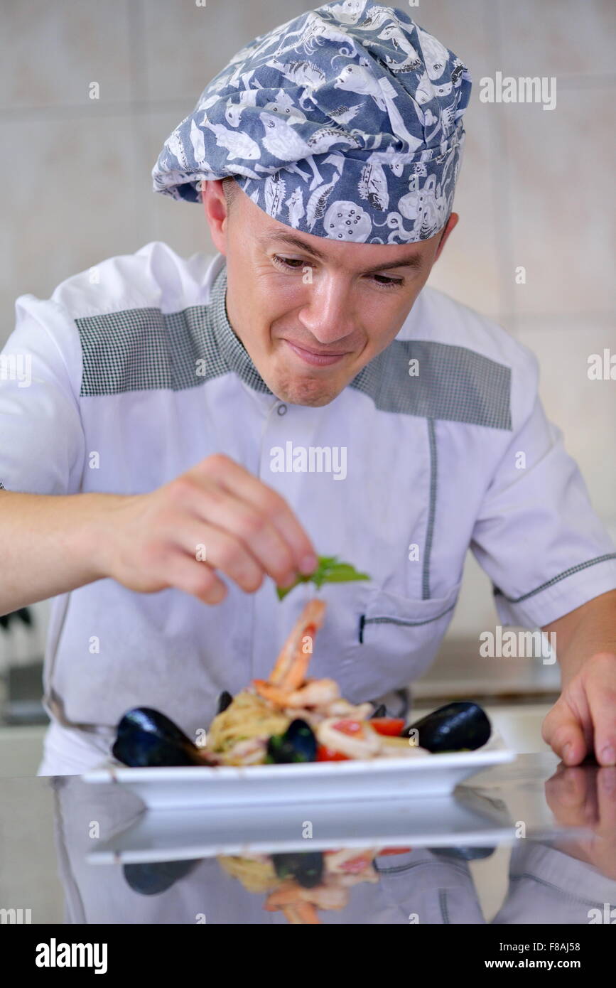Handsome chef dressed in white uniform decorating pasta salad and ...