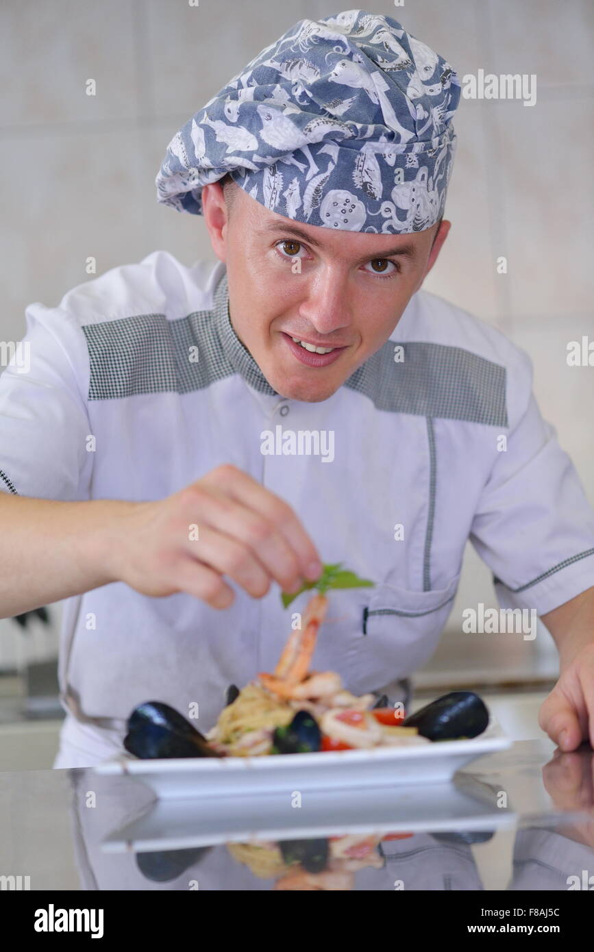 Handsome chef dressed in white uniform decorating pasta salad and ...