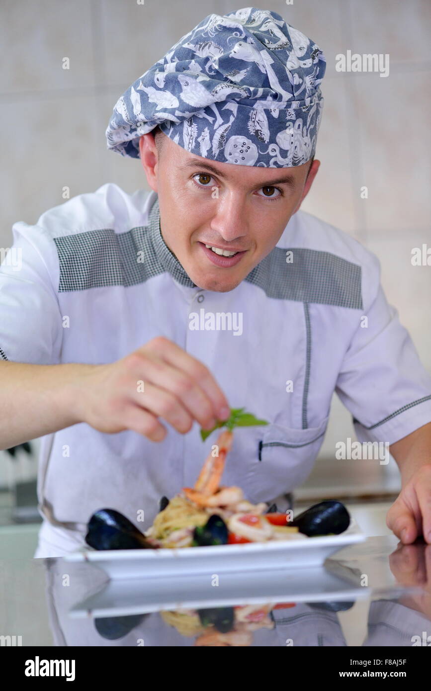 Handsome chef dressed in white uniform decorating pasta salad and ...