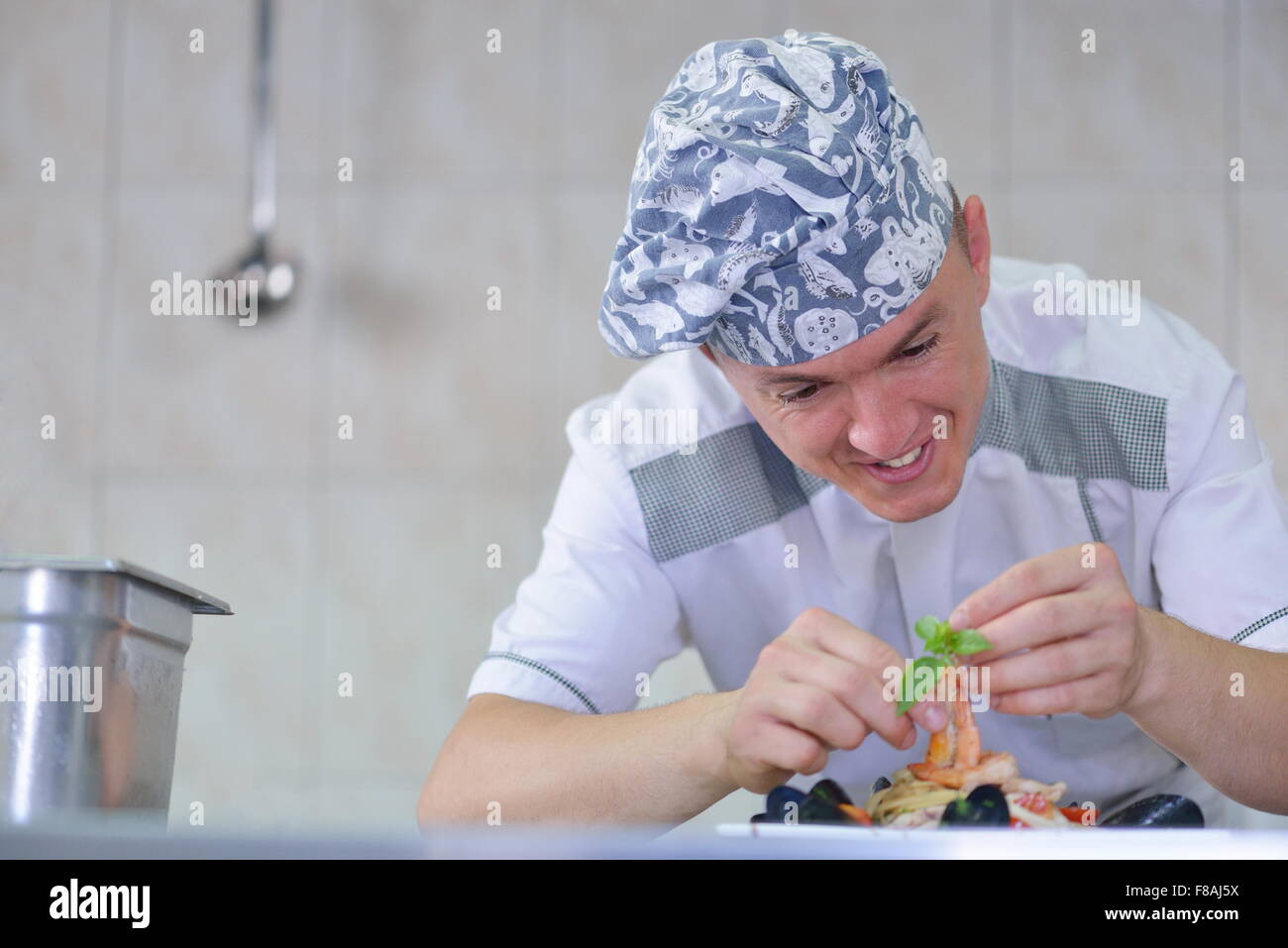 Handsome chef dressed in white uniform decorating pasta salad and ...
