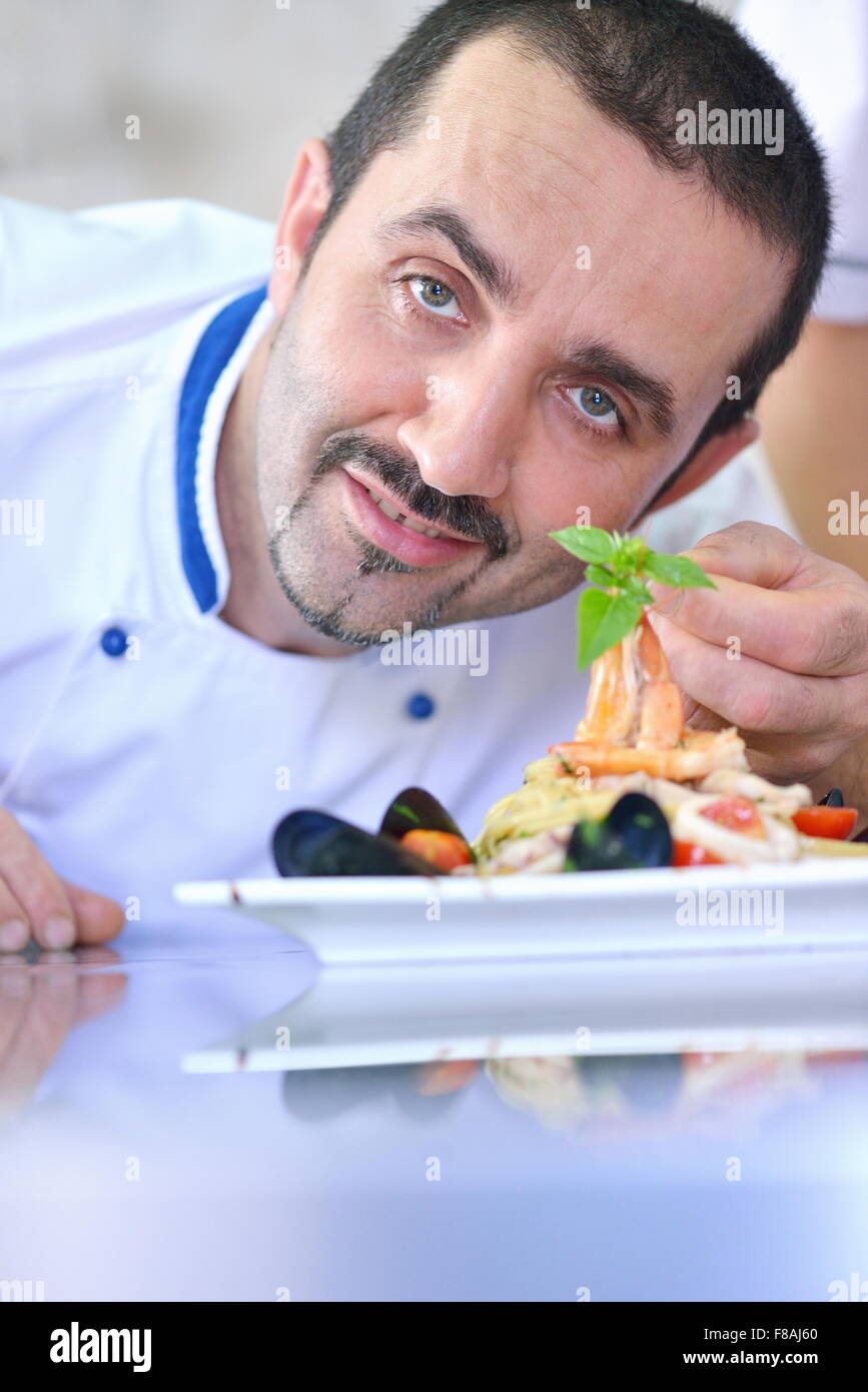 Handsome chef dressed in white uniform decorating pasta salad and ...