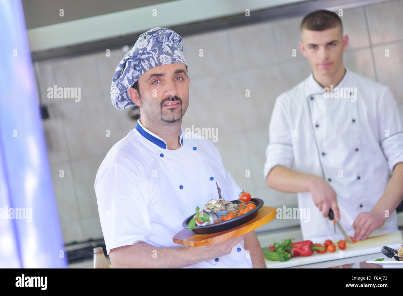 Handsome chef dressed in white uniform decorating pasta salad and ...