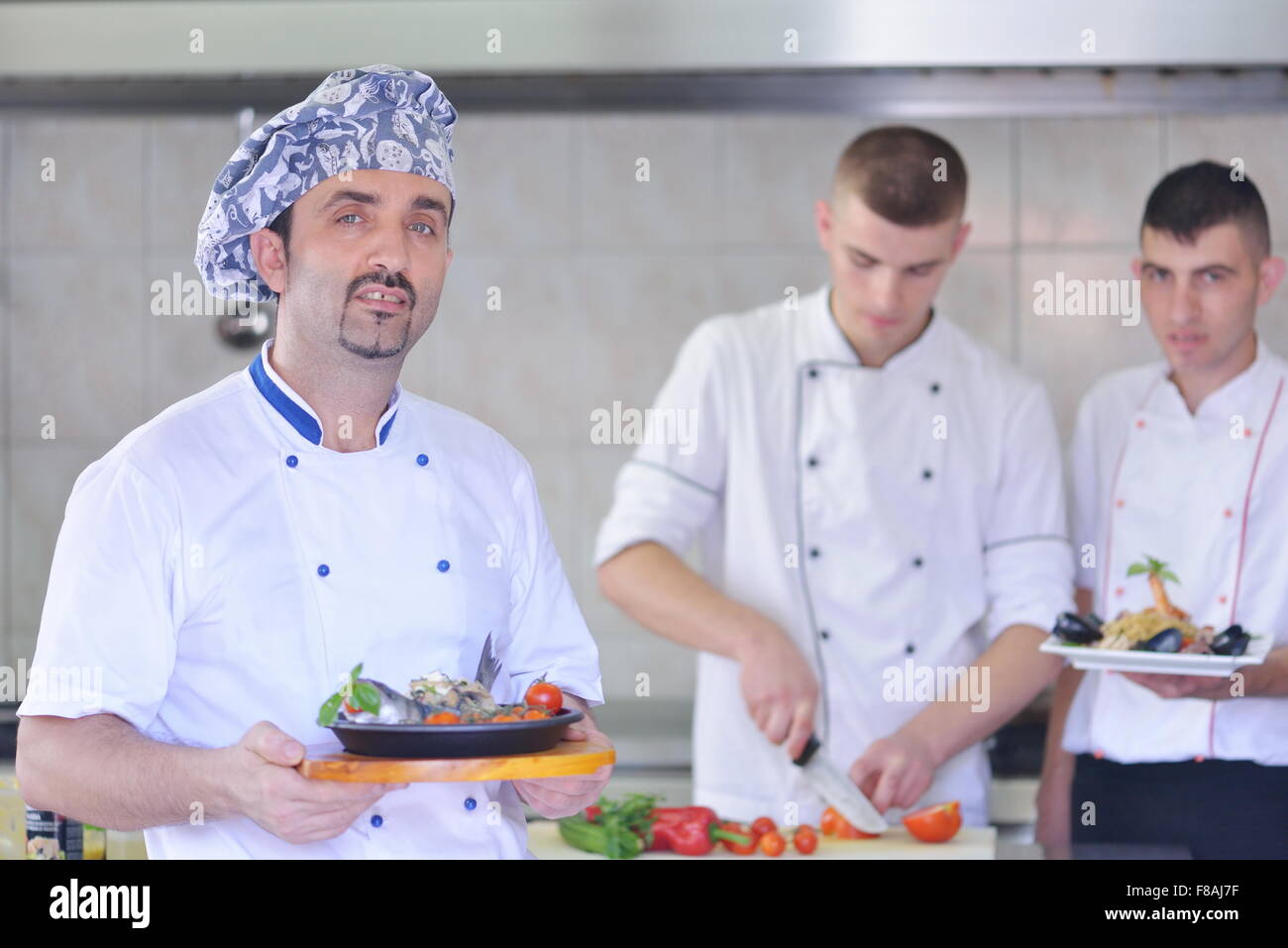 Handsome chef dressed in white uniform decorating pasta salad and ...