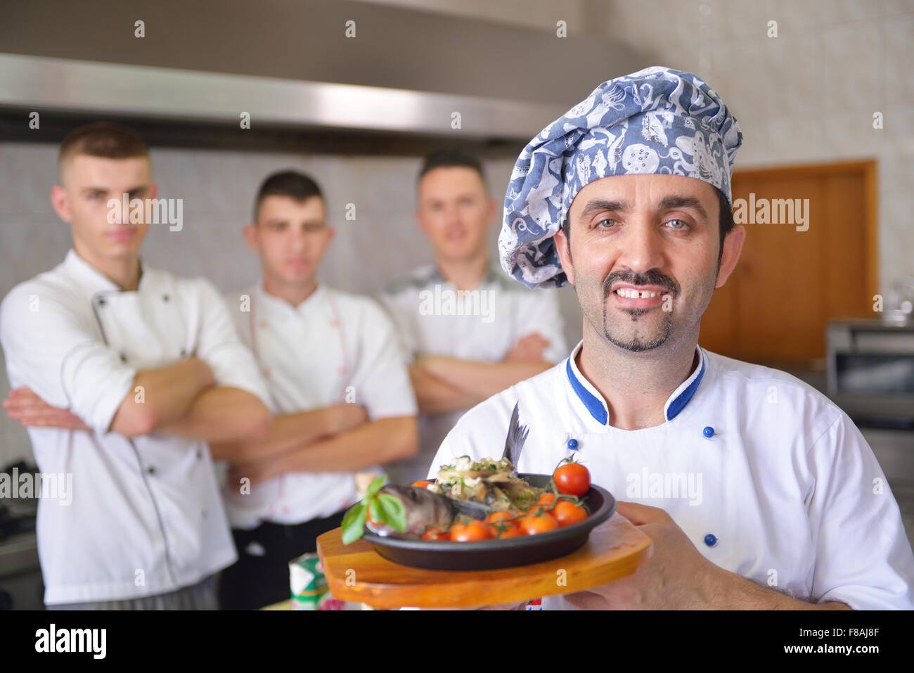 Handsome chef dressed in white uniform decorating pasta salad and ...