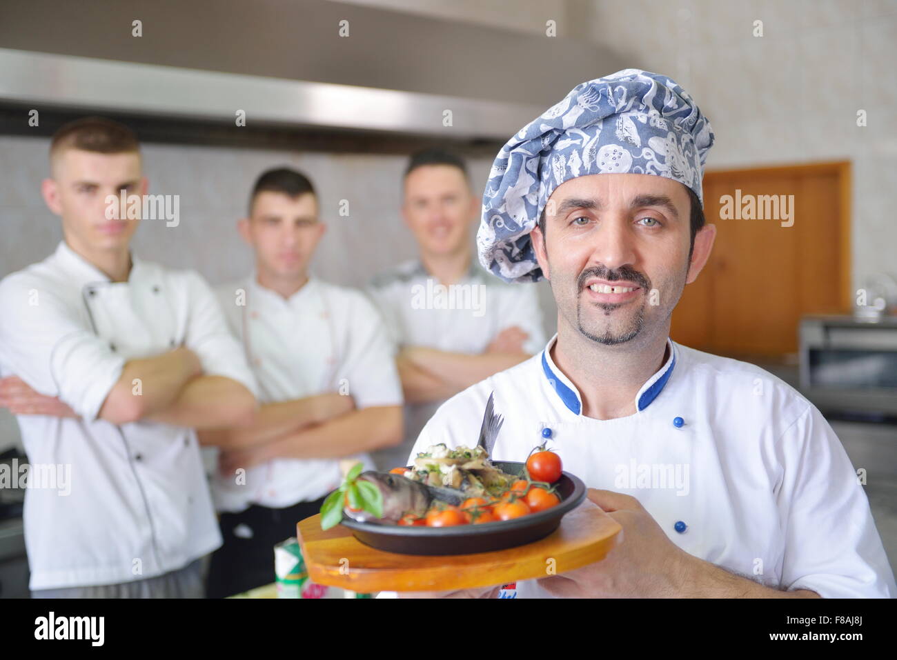 Handsome chef dressed in white uniform decorating pasta salad and ...