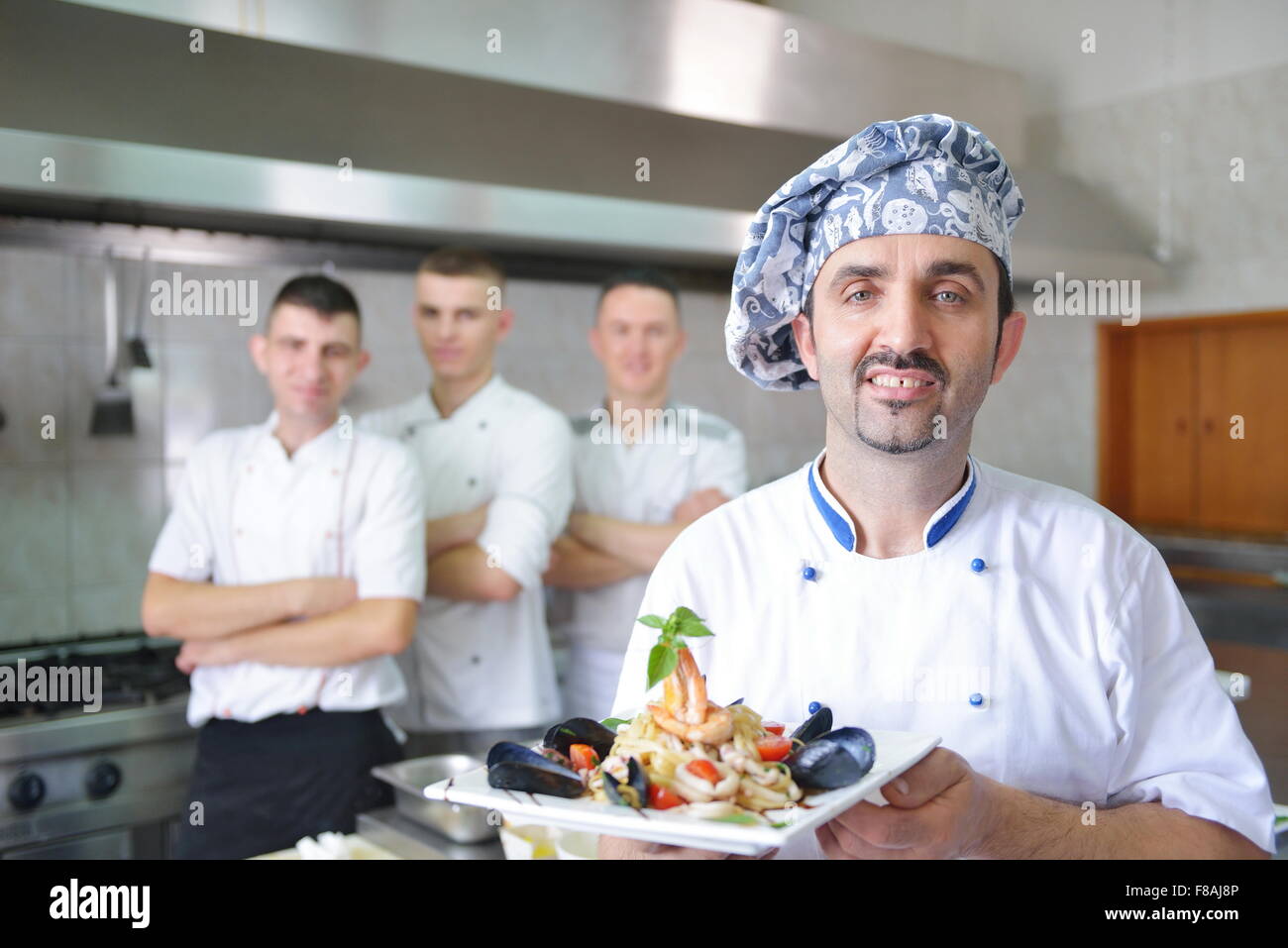 Handsome chef dressed in white uniform decorating pasta salad and ...