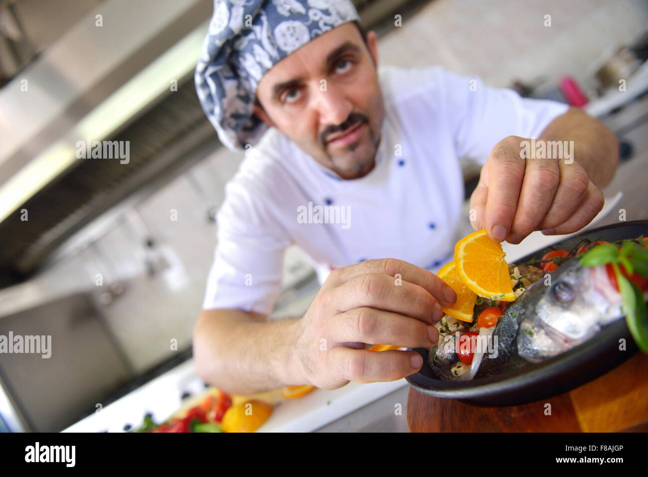 Handsome chef dressed in white uniform decorating pasta salad and ...
