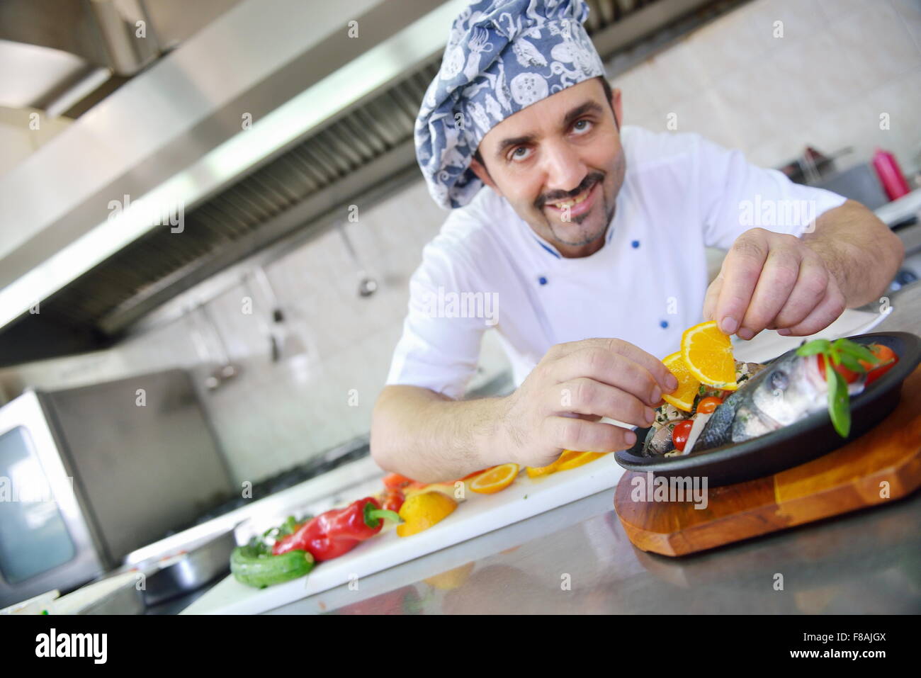 Handsome chef dressed in white uniform decorating pasta salad and ...