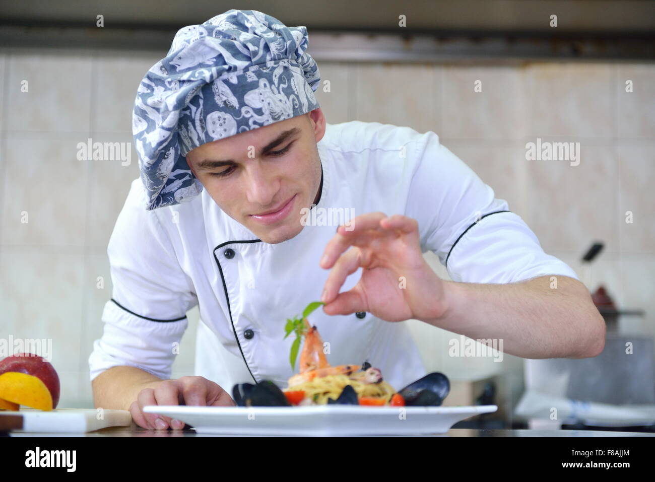 Handsome chef dressed in white uniform decorating pasta salad and ...