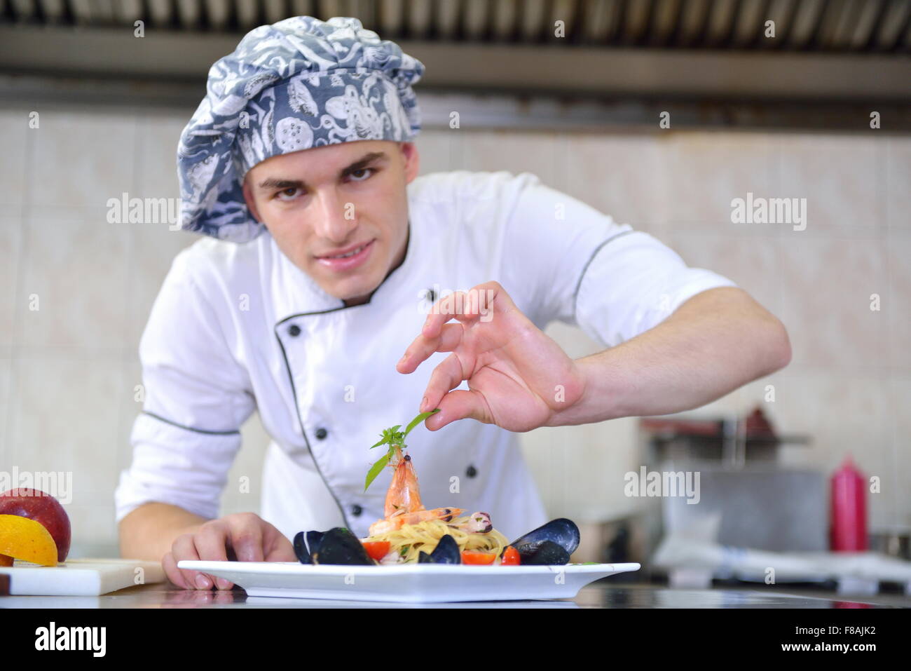 Handsome chef dressed in white uniform decorating pasta salad and ...