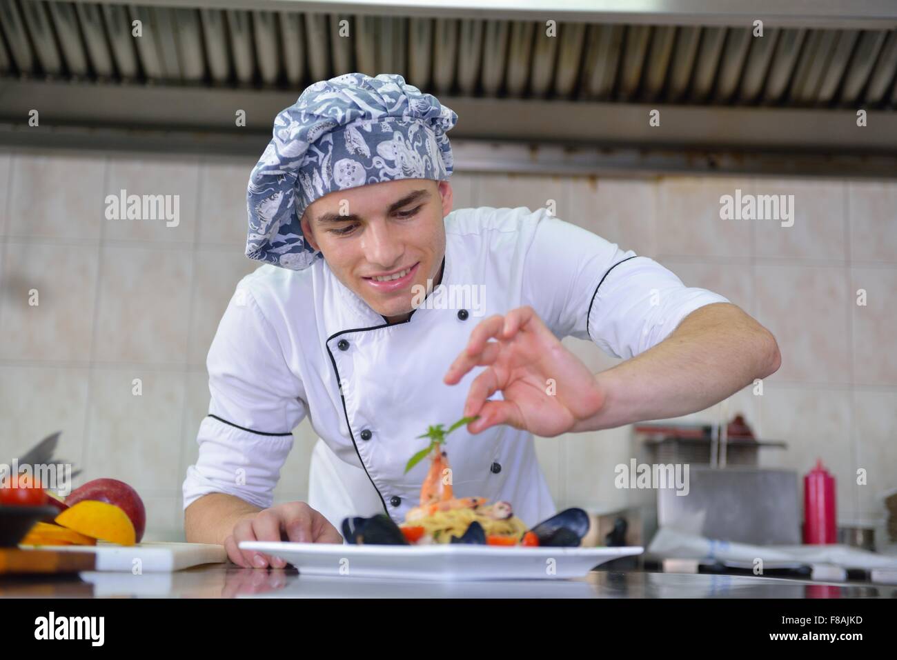 Handsome chef dressed in white uniform decorating pasta salad and ...