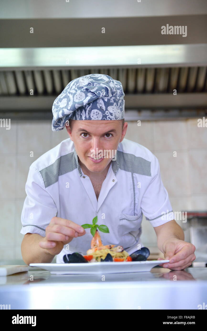 Handsome chef dressed in white uniform decorating pasta salad and ...