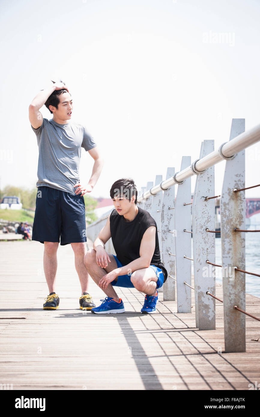Two young men in sportswear taking a rest near the fence at the ...
