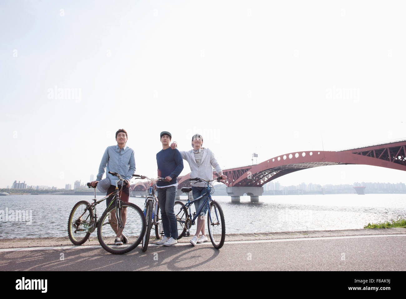 Three young men standing with their bicycles at the riverside near the ...