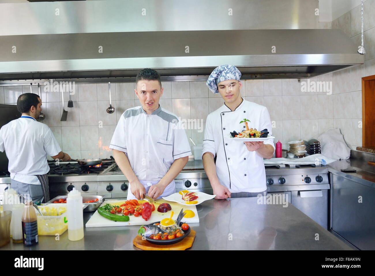 Handsome chef dressed in white uniform decorating pasta salad and ...