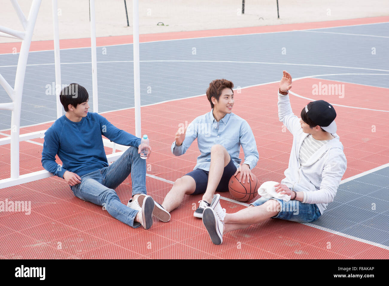 Three young men taking a rest sitting on the basketball court Stock ...