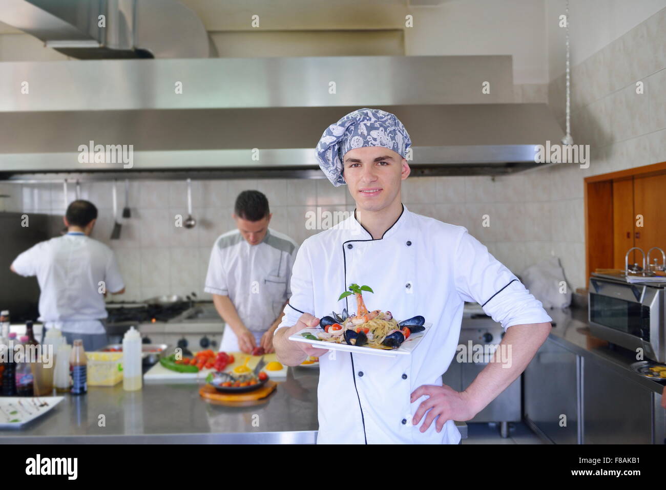 Handsome chef dressed in white uniform decorating pasta salad and ...