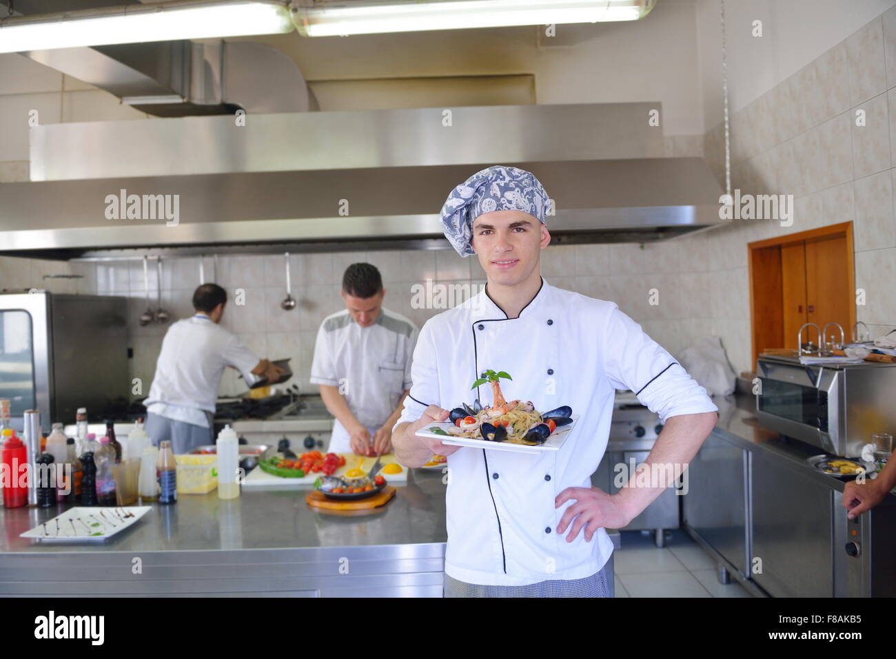 Handsome chef dressed in white uniform decorating pasta salad and ...
