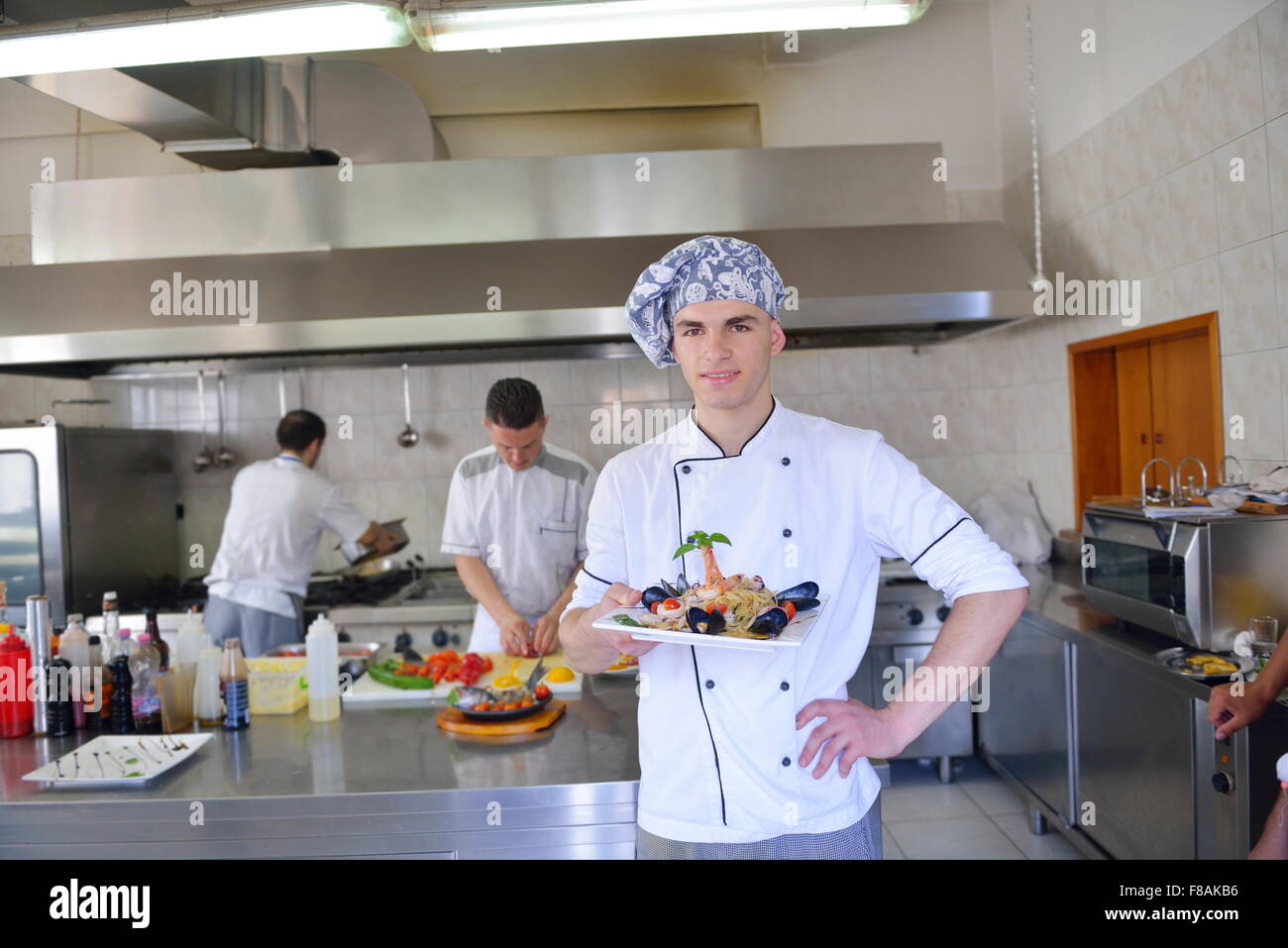 Handsome chef dressed in white uniform decorating pasta salad and ...