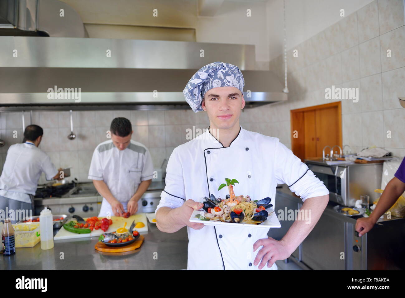 Handsome chef dressed in white uniform decorating pasta salad and ...