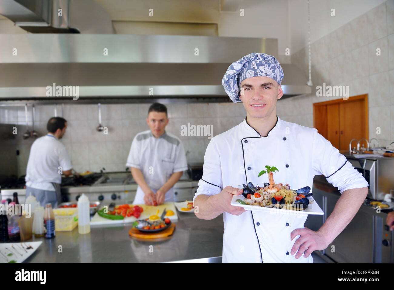 Handsome chef dressed in white uniform decorating pasta salad and ...