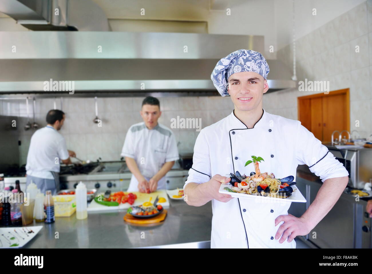 Handsome chef dressed in white uniform decorating pasta salad and ...