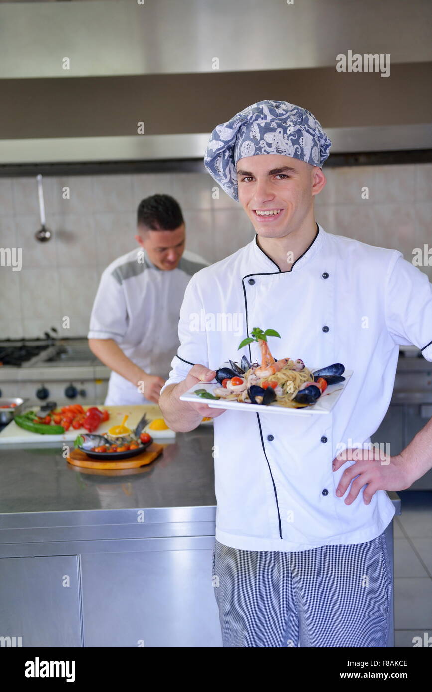 Handsome chef dressed in white uniform decorating pasta salad and ...