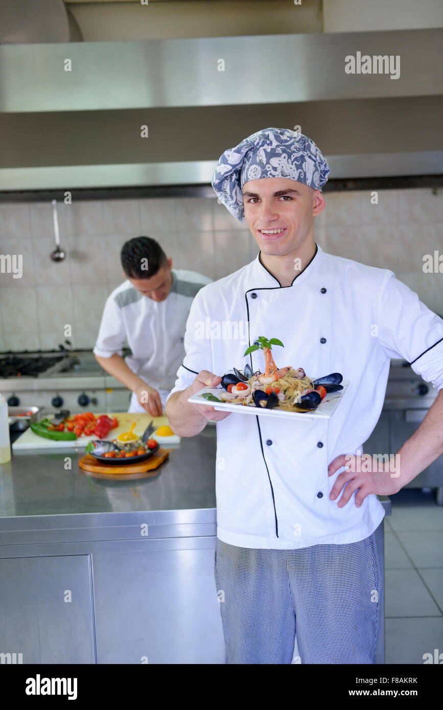 Handsome chef dressed in white uniform decorating pasta salad and ...