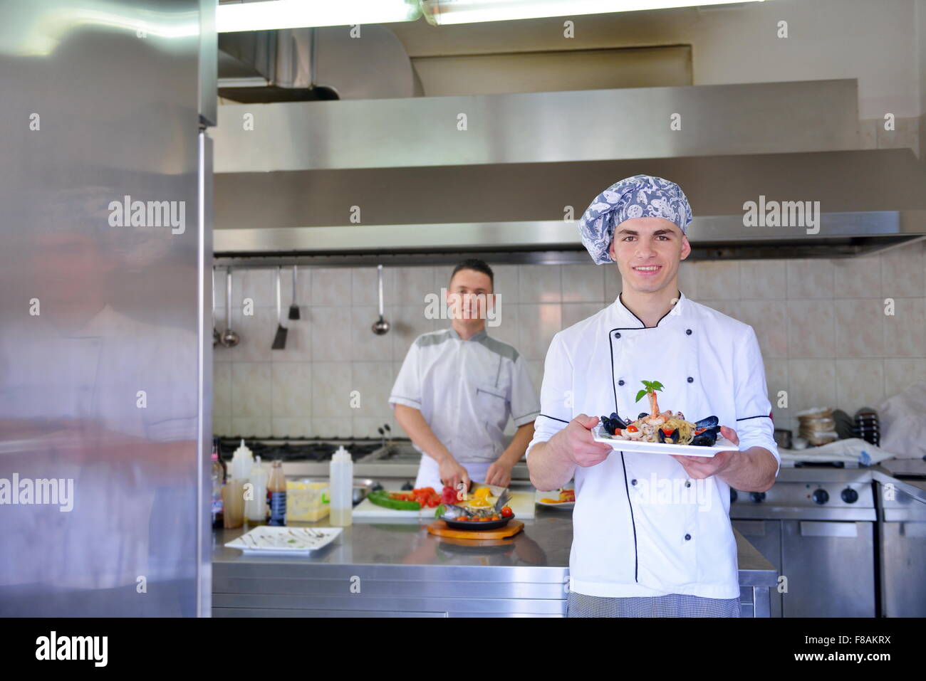 Handsome chef dressed in white uniform decorating pasta salad and ...