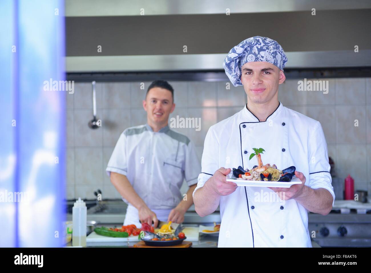 Handsome chef dressed in white uniform decorating pasta salad and ...