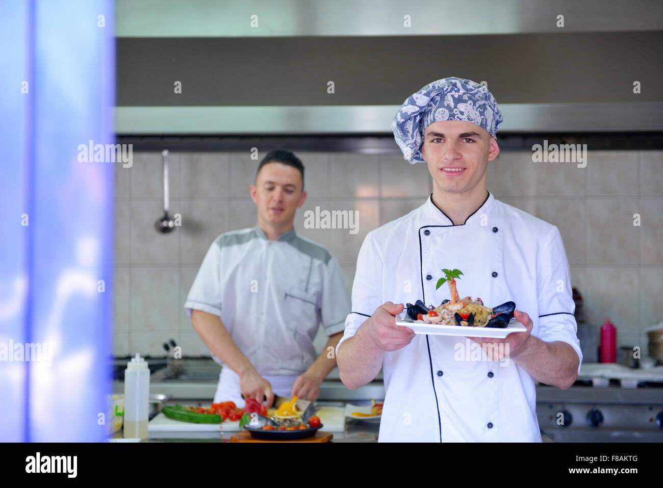Handsome chef dressed in white uniform decorating pasta salad and ...