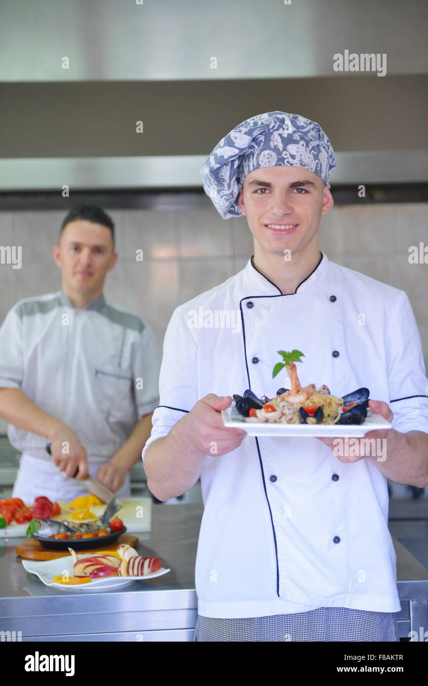 Handsome chef dressed in white uniform decorating pasta salad and ...