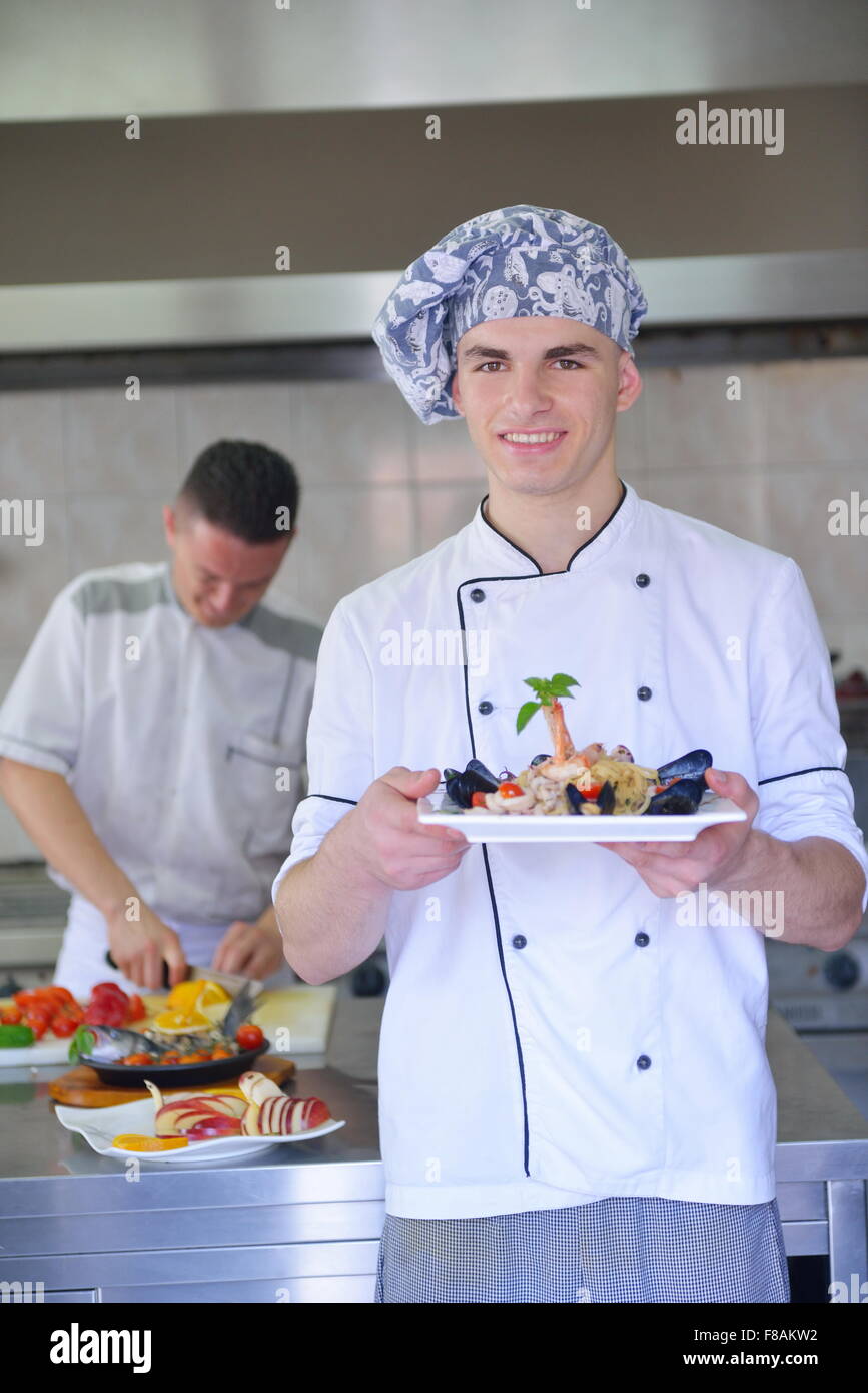 Handsome chef dressed in white uniform decorating pasta salad and ...