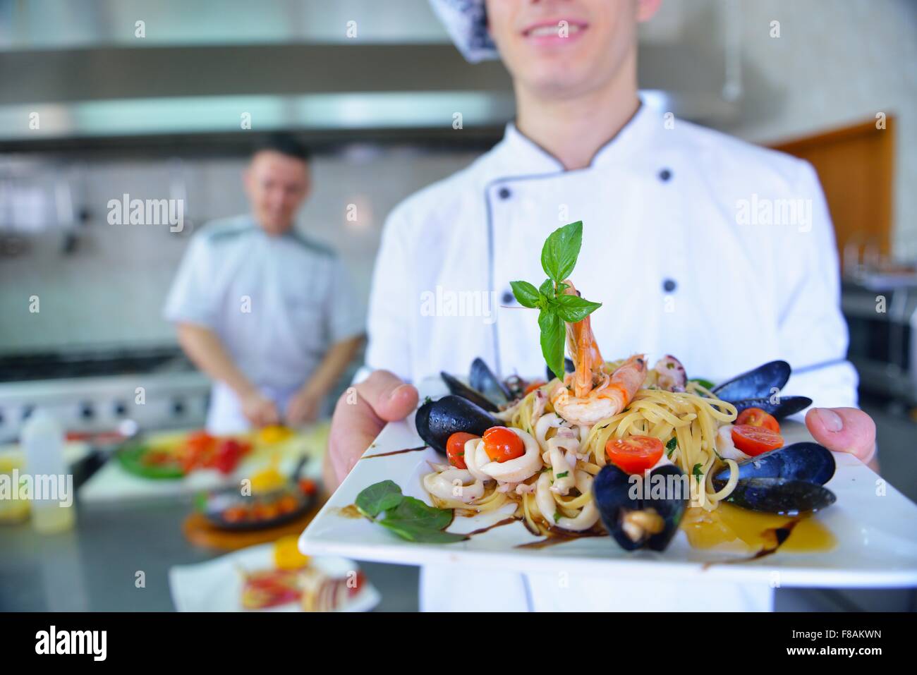 Handsome chef dressed in white uniform decorating pasta salad and ...