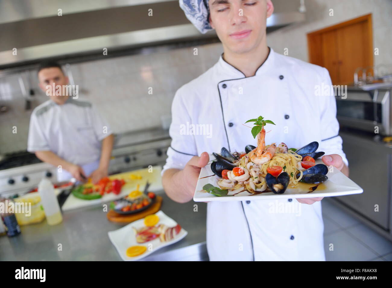 Handsome chef dressed in white uniform decorating pasta salad and ...
